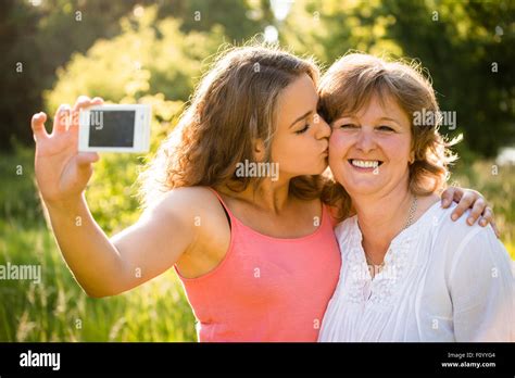 Adult Daughter Kissing Her Senior Mother While Taking Selfie Photo With