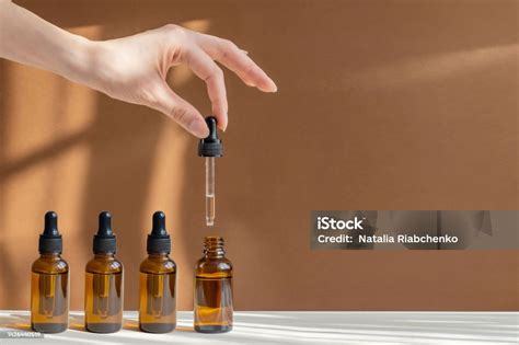 여자의 손은 밝은 갈색 배경의 열린 병 위에 햇빛 광선으로 세럼이 든 피펫을 들고 있습니다 화장품 클로즈업이 있는 표시가 없는