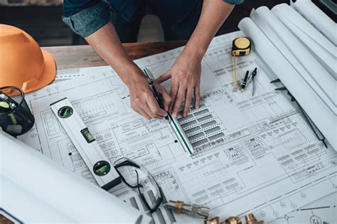 사무실 책상과 계산기 삼각형 눈금자 안전 안경 나침반 블루프린트의 버니어 캘리퍼에서 도면 검사 및 쓰기로 작업하는 엔지니어링 엔지니어 건축가 산업 및 공장 개념 개발에 대한