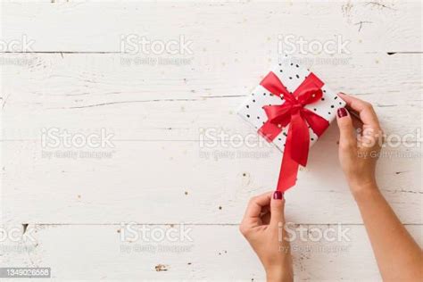 흰색 나무 배경에 빨간 새틴 리본크리스마스 또는 생일 선물 상자를 포장 해제 여성의 손에 최고 보기 나비매듭에 대한 스톡 사진