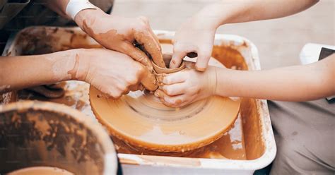 성인과 어린이의 손이 도자기를 만들고 젖은 점토 근접 촬영으로 작업합니다 더러운 손으로 바퀴에 점토로 그릇을 만드는 과정 여름 공원에서 수제 축제 도자기 작업장 사진