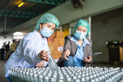 아시아 검사관 감독관 여성은 가공 공장의 창고에서 과일 음료 포장의 재고 제품을 확인하는 멸균 정장을 입은 보조 직원을 가지고