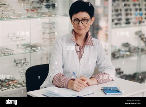 Beautiful Mature Optometrist Writing In Book At Ophthalmology Optician