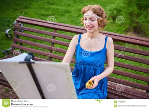 El Muchacha Artista Hermoso En La Calle En Un Vestido Azul Dibuja En El Caballete Imagen De
