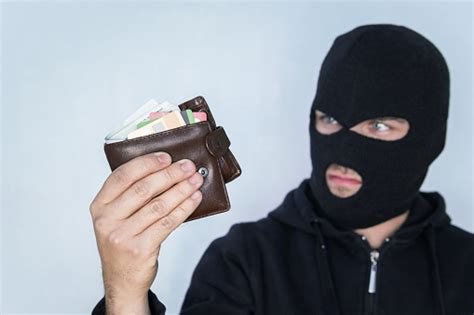 발라클라바의 강도는 도난당한 지갑에 있는 돈을 계산합니다 지갑을 들고 카메라를 보고 검은 마스크에 도둑 가죽에 대한 스톡 사진