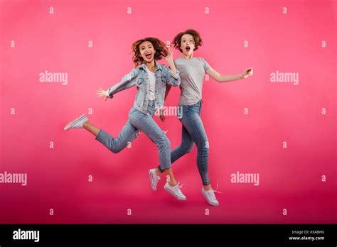 Image Of Two Emotional Ladies Friends Jumping Isolated Over Pink Background Looking Camera