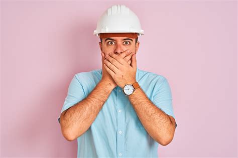 고립된 분홍색 배경 위에 보안 헬멧을 쓰고 있는 젊은 건축가가 실수로 손으로 입을 가리는 충격을 받았다 비밀 개념입니다 건설 산업에 대한 스톡 사진 및 기타 이미지 Istock
