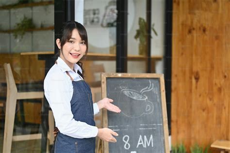 Foto Mujer Sonriente Dueña De Una Cafetería De Pie En La Puerta Con Una