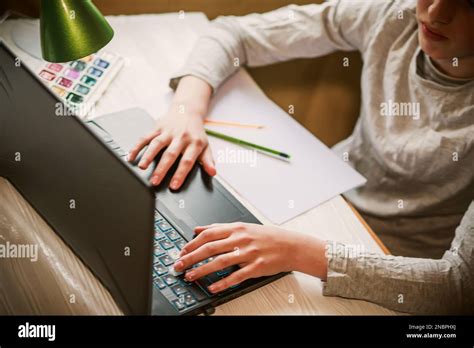 The Boy Writes Down The Task On A Blank Sheet Lying Near The Laptop