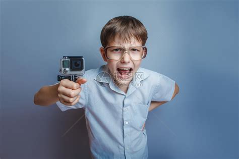 一个10年欧洲外貌的男孩戴眼镜拿着相机双手握着照相机在灰色高清图片下载 正版图片502972050 摄图网