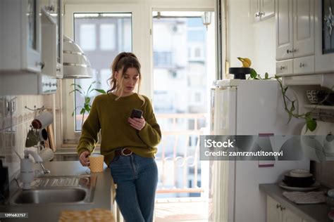 부엌에 서서 스마트 폰을 사용하는 동안 차 한 잔을 마시는 여성 가정 생활에 대한 스톡 사진 및 기타 이미지 가정 생활