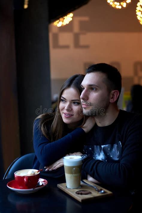 Young Happy Man And Woman Sitting At The Table In Coffee Shop Hugging