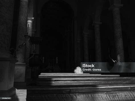 Lady With White Hair Praying Sitting In A Very Dark And Antique Church