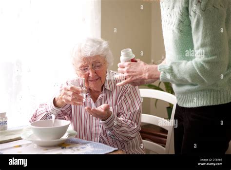 Female Caregiver Helping And Elderly Woman Taking Her Medication Stock