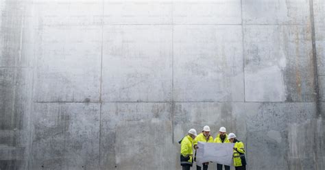 건설 현장의 콘크리트 벽에 기대어 청사진을 들고 서 있는 엔지니어 그룹 공간을 복사합니다 사진 Unsplash의 노동자 이미지