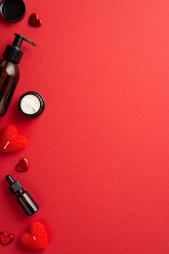 유기농 화장품 개념입니다 호박색 유리 펌프 병 스포이드 병 크림 항아리 심장 모양의 양초와 색종이의 상위 뷰 수직 사진 복사 공간이 있는 격리된 빨간색 배경에 밸런타인데이에