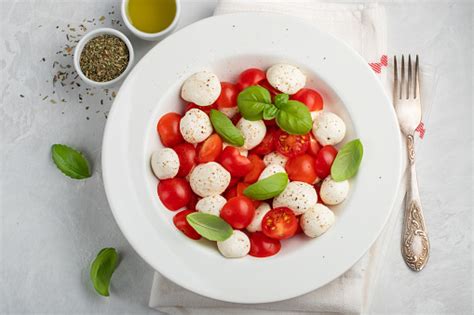 잘 익은 토마토 모 짜 렐 라와 신선한 바 질 맛 있는 클래식 Caprese 샐러드의 흰색 접시 회색 콘크리트 바탕에 나뭇잎