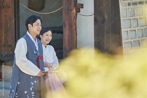 한복을 입고 한국의 전통 가옥 노란꽃 흐린배경 담장을 배경으로 커플 여행자 아름답고 멋진 젊은 아시아 한국 남녀 모델 foto