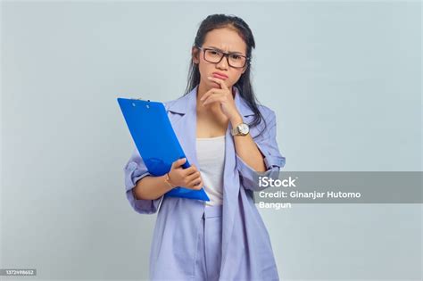 심각한 젊은 아시아 비즈니스 여성이 턱을 잡고 보라색 배경에 고립 된 문서 폴더를 들고있는 동안 무언가를 숙고하는 초상화 25
