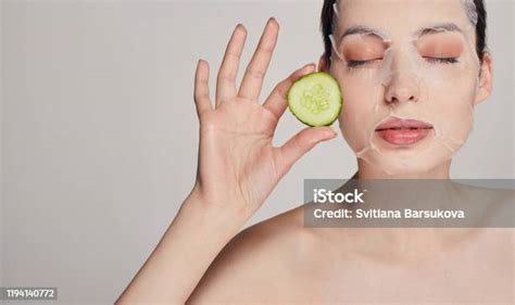 눈을 감고 손이 그녀의 얼굴 근처 양손에 오이를 보유하고 심각한 배경에 얼굴에 신선한 오이와 보습 마스크에 아름다움 소녀 건강