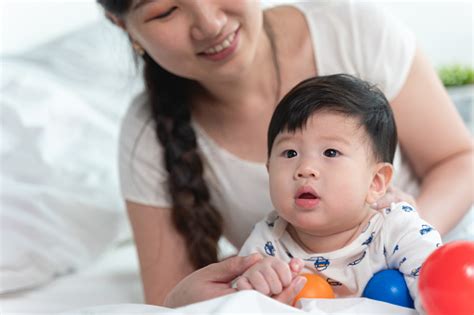 젊은 아름다운 아시아 어머니는 침대에 아시아 아기와 함께 장난감 공을 함께 화이트 침대에 행복하고 쾌활한 느낌과 침대에서 기어