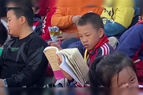 人群中，孩子们都在休息闲聊，小男生拿着一本书认真读着男生人群