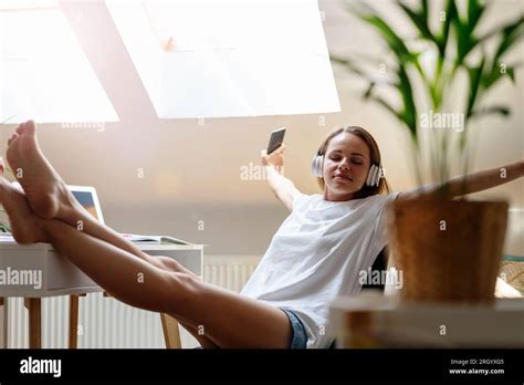 Young Woman Sits With Her Feet Up On The Table Listens To Music Using