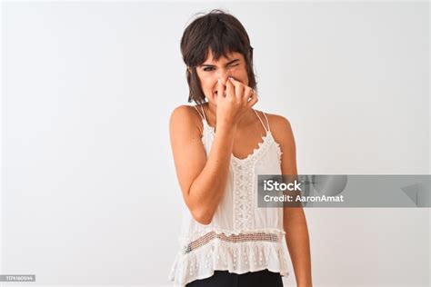 여름 캐주얼 티셔츠를 입고 고립 된 흰색 배경 위에 서있는 젊은 아름다운 여성은 냄새가 없고 역겨운 냄새 참을 수없는 냄새를 맡고 코에 손가락으로 숨을 들고 있습니다 나쁜