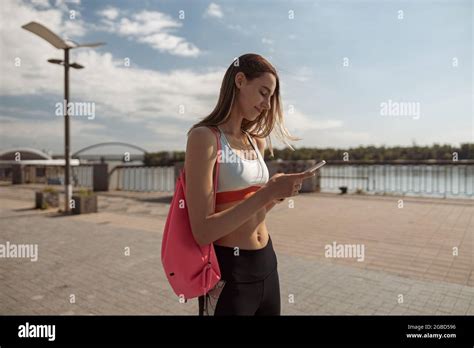 Positive Woman In Stylish Tracksuit Uses Mobile Phone Standing On City