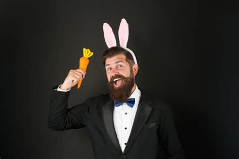 당근을 곁들인 신사 부활절 토끼 검은 배경 수염을 기리는 남자는 당근을 들고 있다 행복한 우아한 사업가는 토끼 귀를 착용합니다