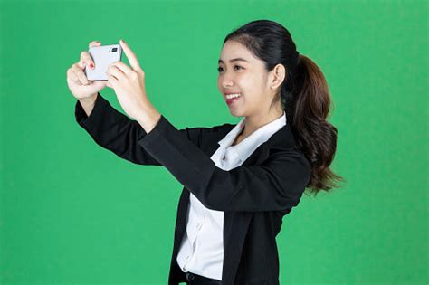 녹색 고립 된 배경에 휴대 전화와 함께 사진이나 셀카를 찍고 젊은 아시아 비즈니스 여성 미소 개성 개념에 대한 스톡 사진 및