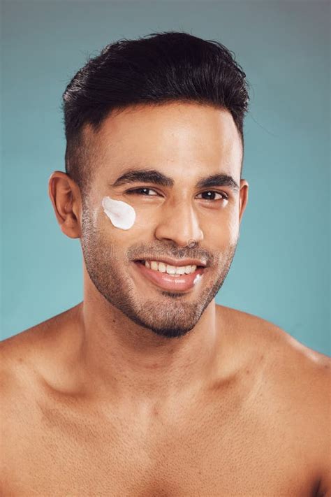 Portrait Of One Smiling Young Indian Man Applying Moisturiser Lotion To His Face While Grooming