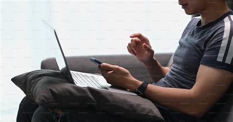 집에서 소파에 앉아 컴퓨터 노트북으로 작업하고 스마트폰을 사용하는 청년의 측면 모습 사진 Unsplash의 태국 이미지