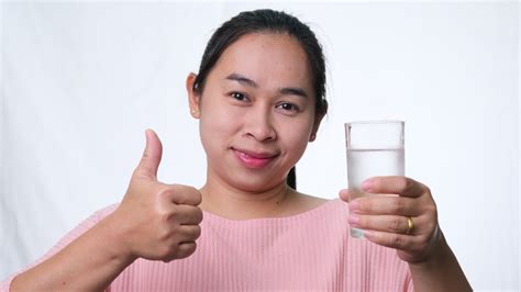 Smiling Woman Holding A Glass Of Water And Thumbs Up On White