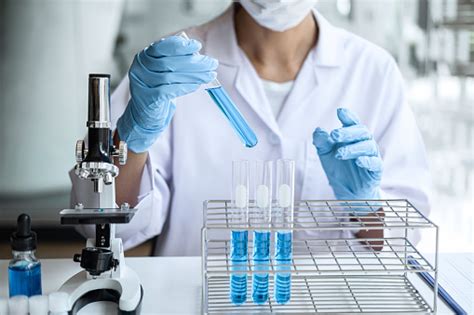 실험실에서 일하는 유리 장비에 색깔 액체의 투하를 가진 현미경 시약을 사용하여 시험관을 들고 있는 실험실 코트에서 생화학 실험실