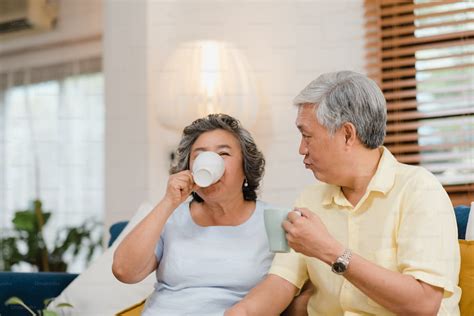 아시아 노부부는 따뜻한 커피를 마시고 집 거실에서 함께 이야기를 나누고 부부는 집에서 휴식을 취할 때 소파에 누워 사랑의