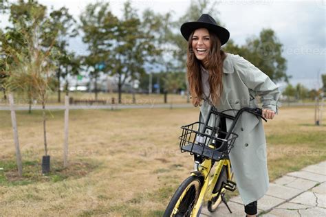 A Young Woman Laughs While Sitting On A Bicycle While Walking Around The City In A Black Hat And
