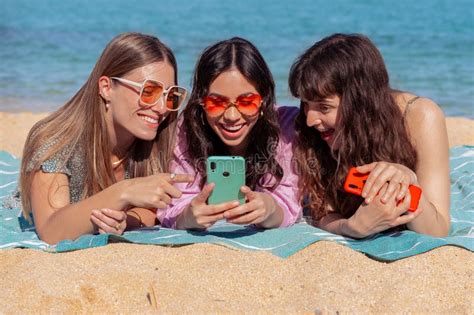 Three Happy Young Friends On The Beach Using Apps On Their Smartphones