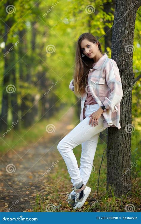 Blonde Female In Blue Dress Leaning Against A Tree Trunk In Autumn Linden Tree Alley Stock Photo