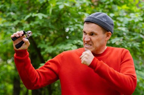 A Man Strengthens His Grip Using A Hand Expander In An Outdoor Forest Setting He Is Seen