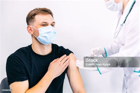 안전 마스크와 보호 장갑을 착용한 여성 간호사가 코로나19 팬데믹 기간 동안 의료 센터에서 남성 환자에게 백신 주사를 맞고 있다 바늘과 주사기를 사용하여 약을 주사하는 의사