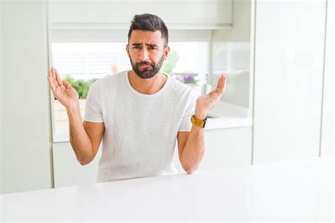 잘 생긴 히스패닉 남자 캐주얼 흰색 티셔츠 집에서 단서와 팔과 손을 제기 와 혼란 표정 의심 개념 T 셔츠에 대한 스톡 사진 및