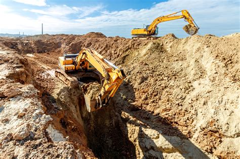 두 대의 굴삭기가 하얀 솜털 구름과 함께 하늘을 배경으로 건설 현장에서 흙을 파고 있습니다 0명에 대한 스톡 사진 및 기타 이미지 0명 개발 건설 산업 Istock