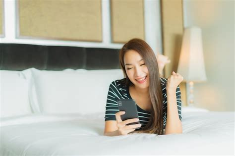 세로 아름 다운 젊은 아시아 여자 침실 인테리어에 침대에 스마트 휴대 전화를 사용 무료 사진