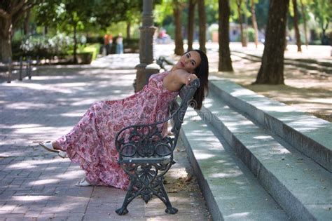 A Young Beautiful Brunette Woman Is Sitting On A Park Bench Her Arms