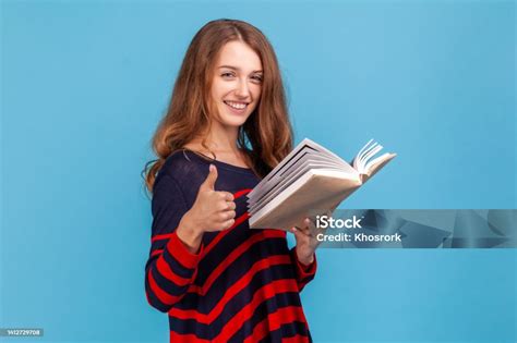 손에 책을 들고 서서 훌륭한 음모로 흥미로운 소설을 읽고 엄지 손가락을 보여주는 여자 읽기에 대한 스톡 사진 및 기타 이미지