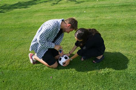 한 남자와 한 여자가 공원의 푸른 잔디 위에 무릎을 꿇고 맑고 푸른 하늘 아래에서 축구공에 공기를 주입하기 위해 함께 일하고 있습니다 그들의 장난기 넘치는 상호 작용은
