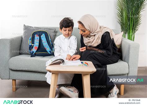 أم عربية خليجية سعودية محجبة تساعد طفلها في التعلم بالمنزل، ايماءات وجه سعيدة، الانشطة التعليمية