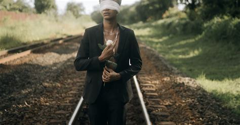Blindfolded Man Standing Barefoot On The Railway Tracks And Holding A