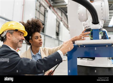 Technician Analyzing Robotic Arm Standing By Engineer In Factory Stock